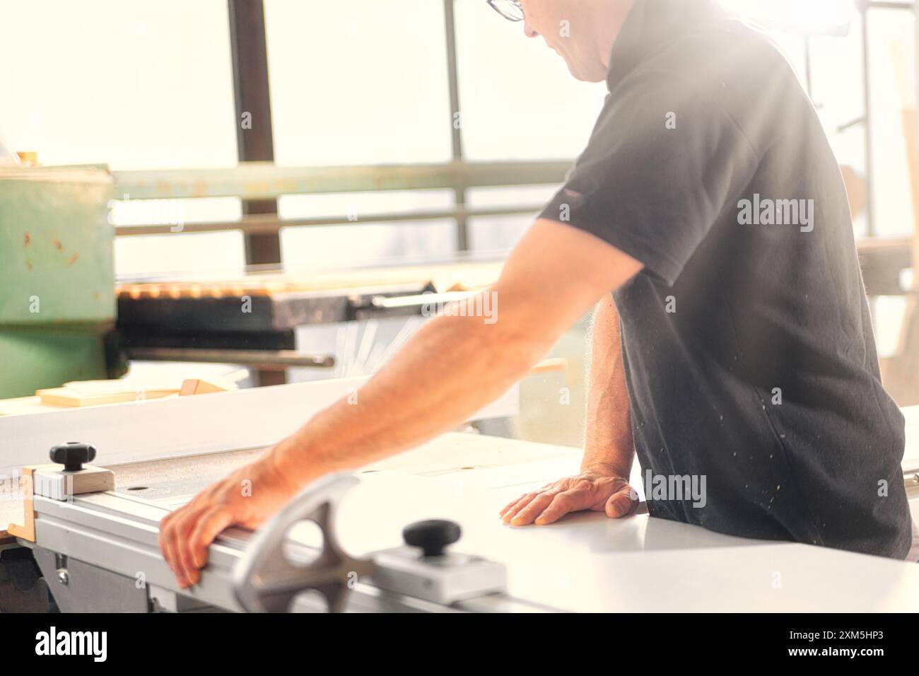 Carpenter is carefully positioning a wood plank on a sawing machine ...