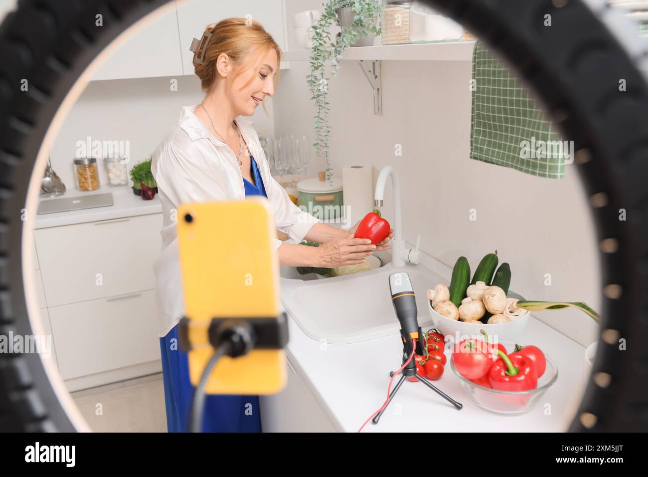 Mature woman washing bell pepper while recording cooking video class in ...