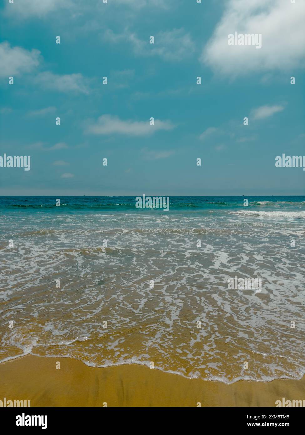 Wave washing up onto sandy beach under a blue sky Stock Photo - Alamy