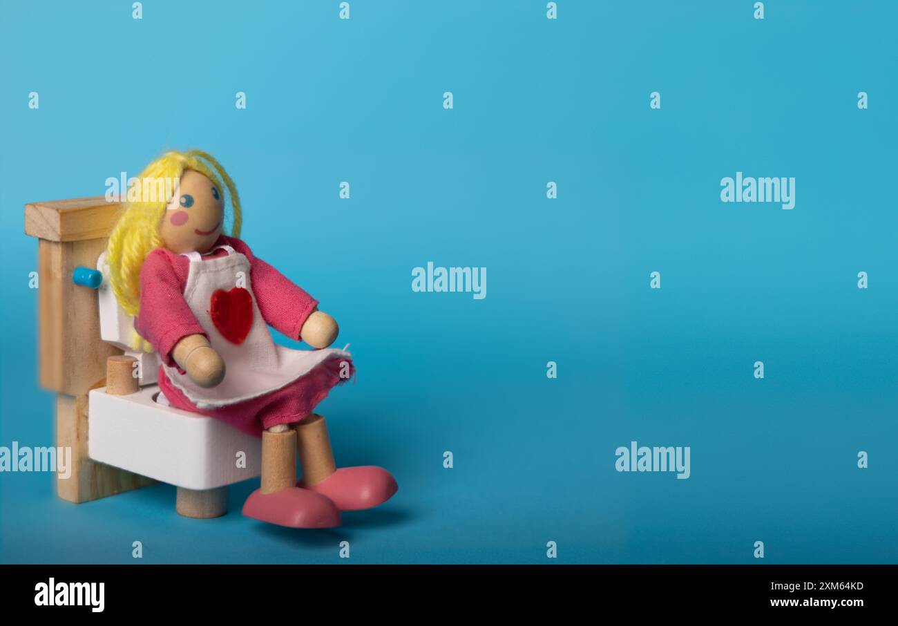 Wooden toy of a woman sitting on a toilet against a simple backdrop. A ...