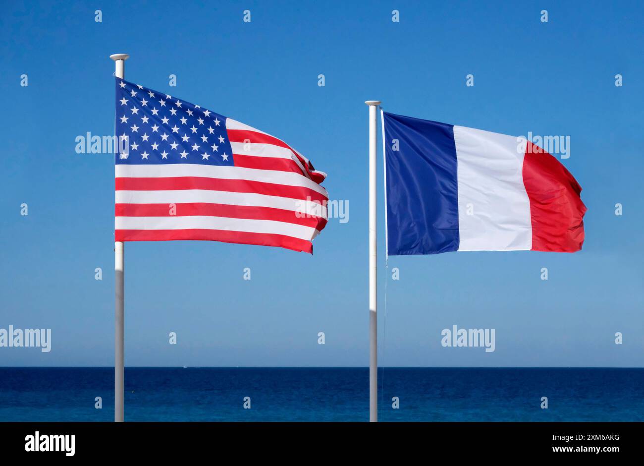 The national flags of the United States and France next to the ocean on ...