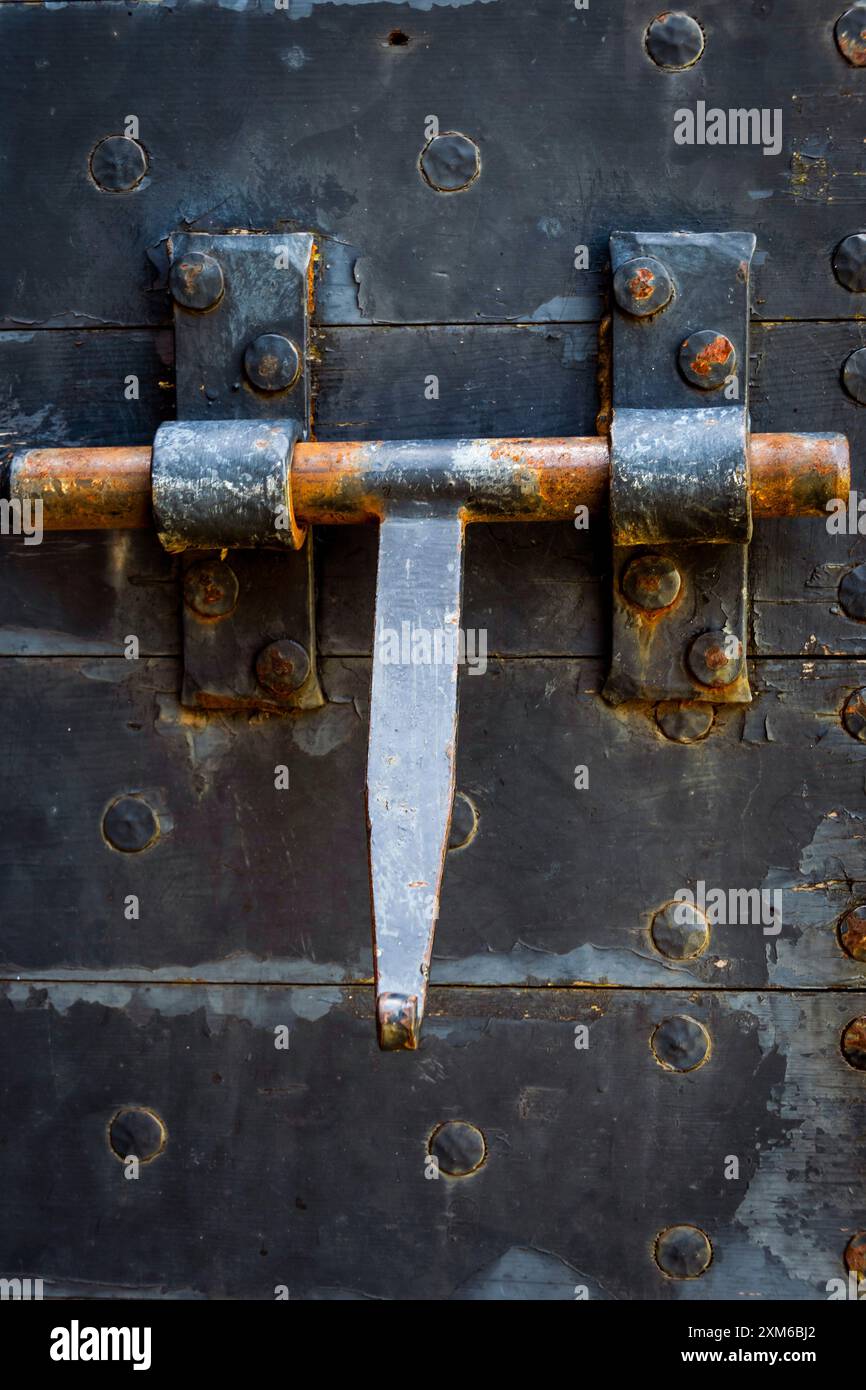 A close-up of a rusty metal door bolt locked into place on an old, dark ...