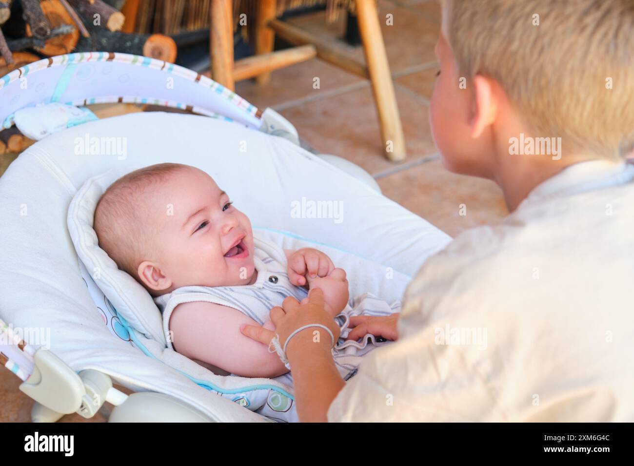 Happy baby boy is lying in bouncer and playing with his brother Stock ...