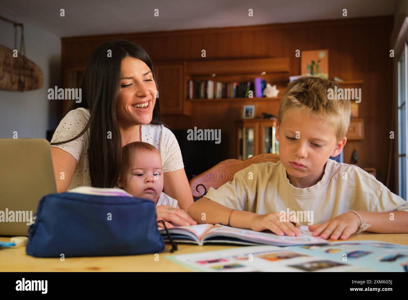 Young boy doing homework with mother and baby boy at home Stock Photo ...