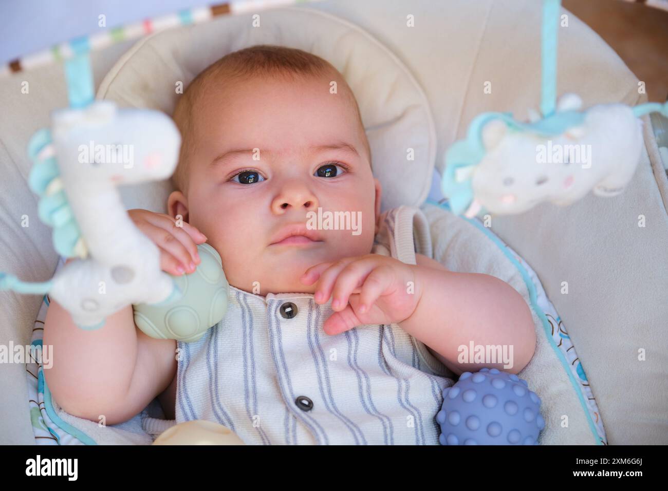 Baby boy playing with sensory toys while relaxing in bouncer Stock ...