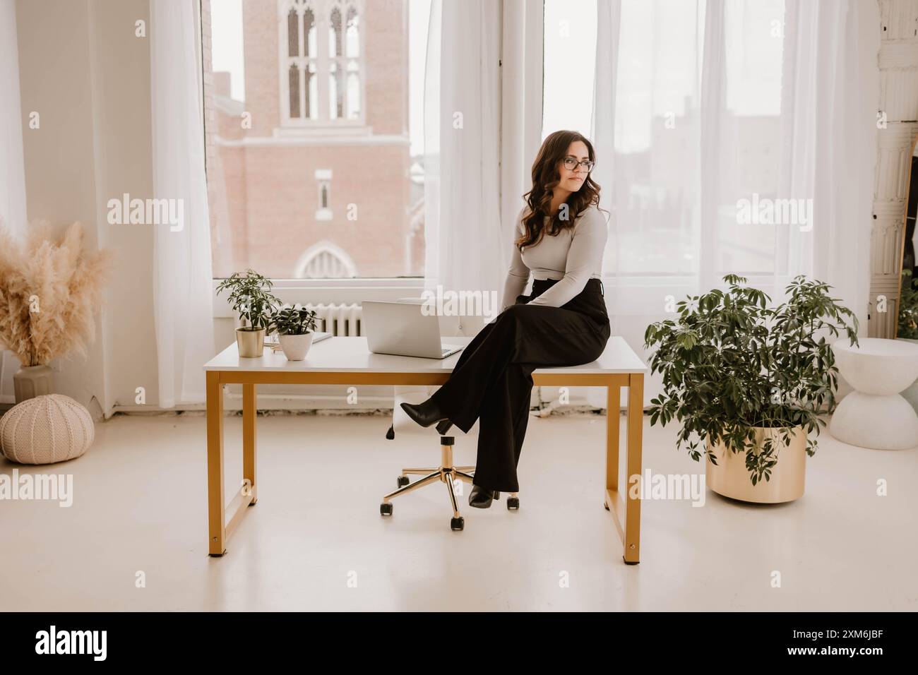 Young Hispanic woman sitting on modern desk with a laptop Stock Photo ...