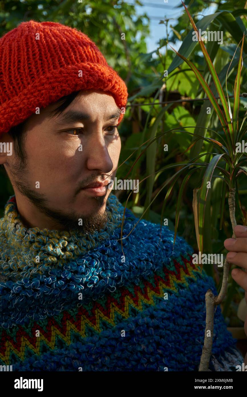 a man in a poncho looks at a plant Stock Photo - Alamy