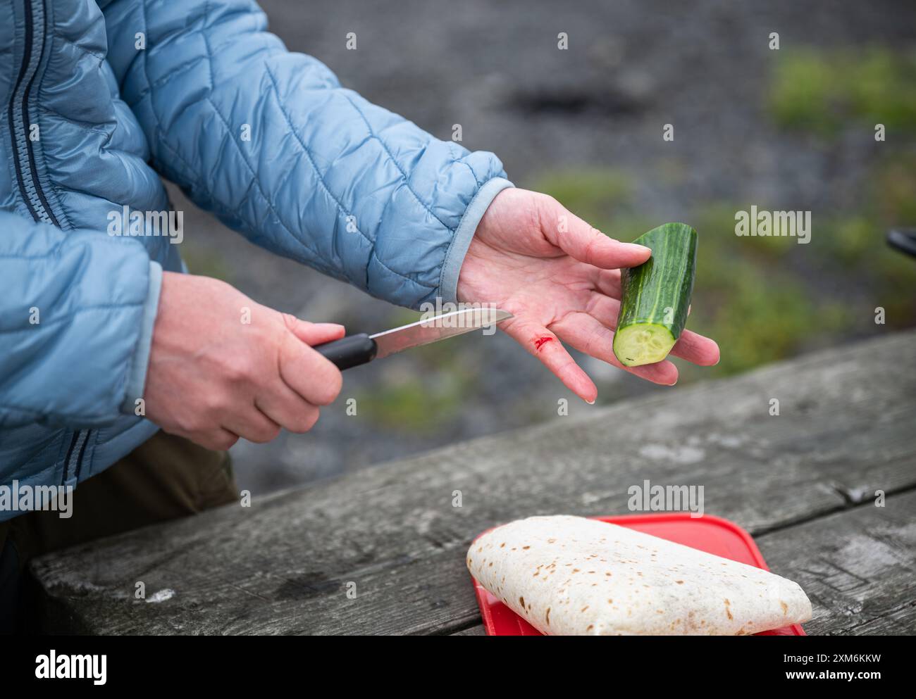 Woman cut finger with knife while cutting cucumber on picnic table ...