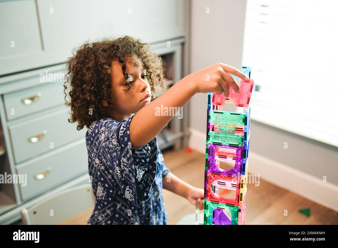 Young girl carefully placing a block on a colorful tower Stock Photo ...
