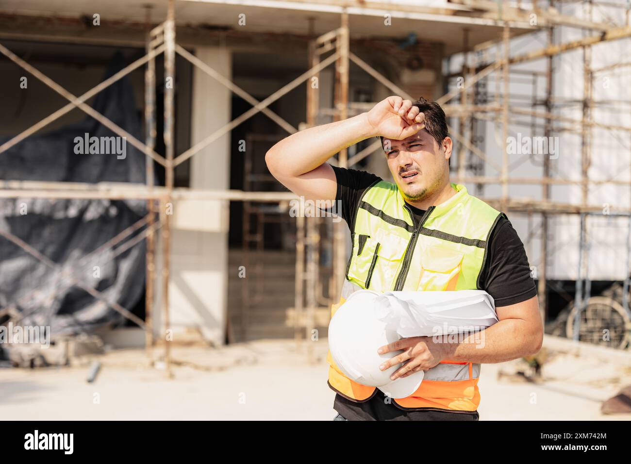 Construction worker taking a break and sweating under the sun, holding ...