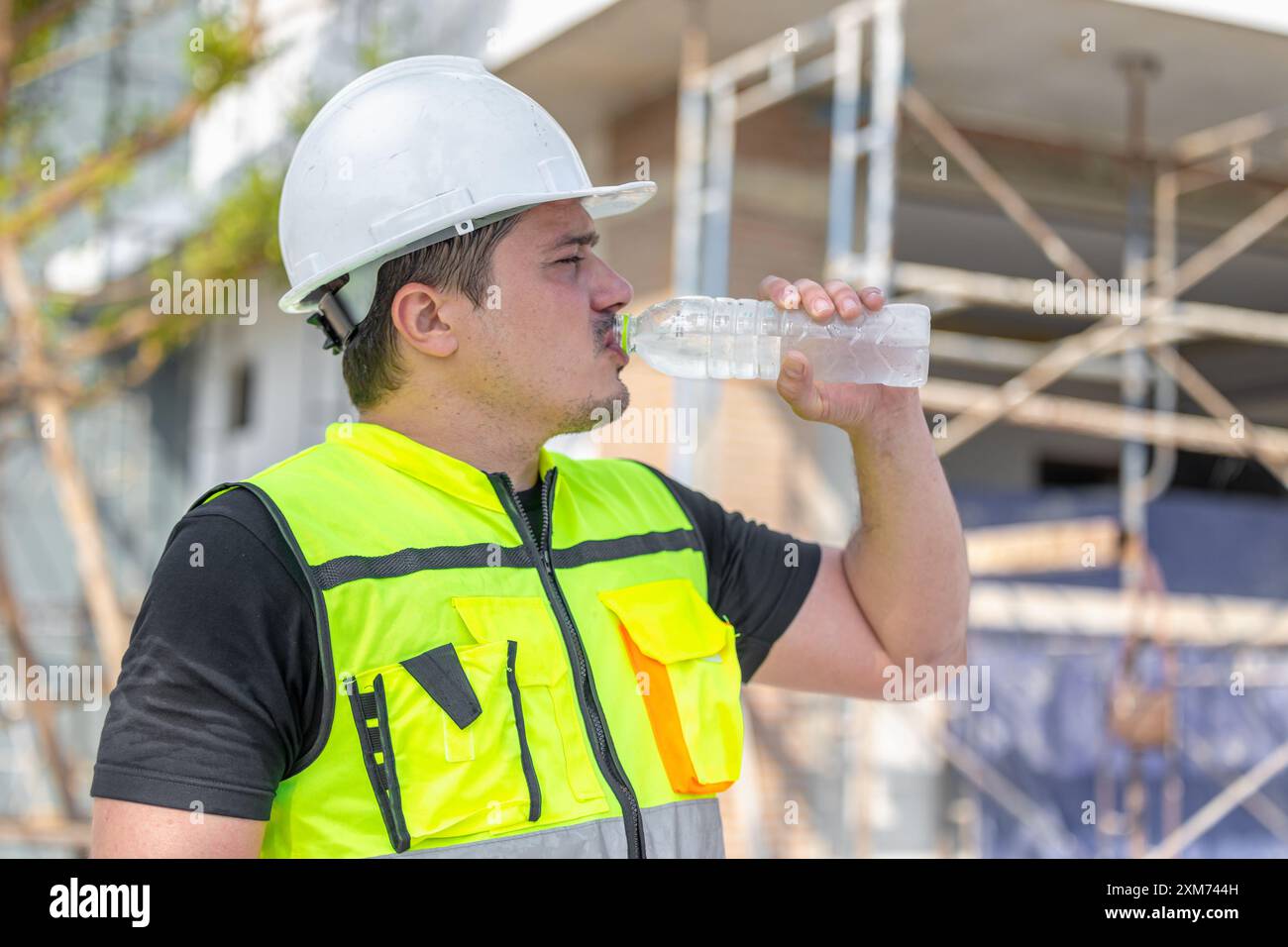 Construction worker in a hard hat and safety vest drinking water ...