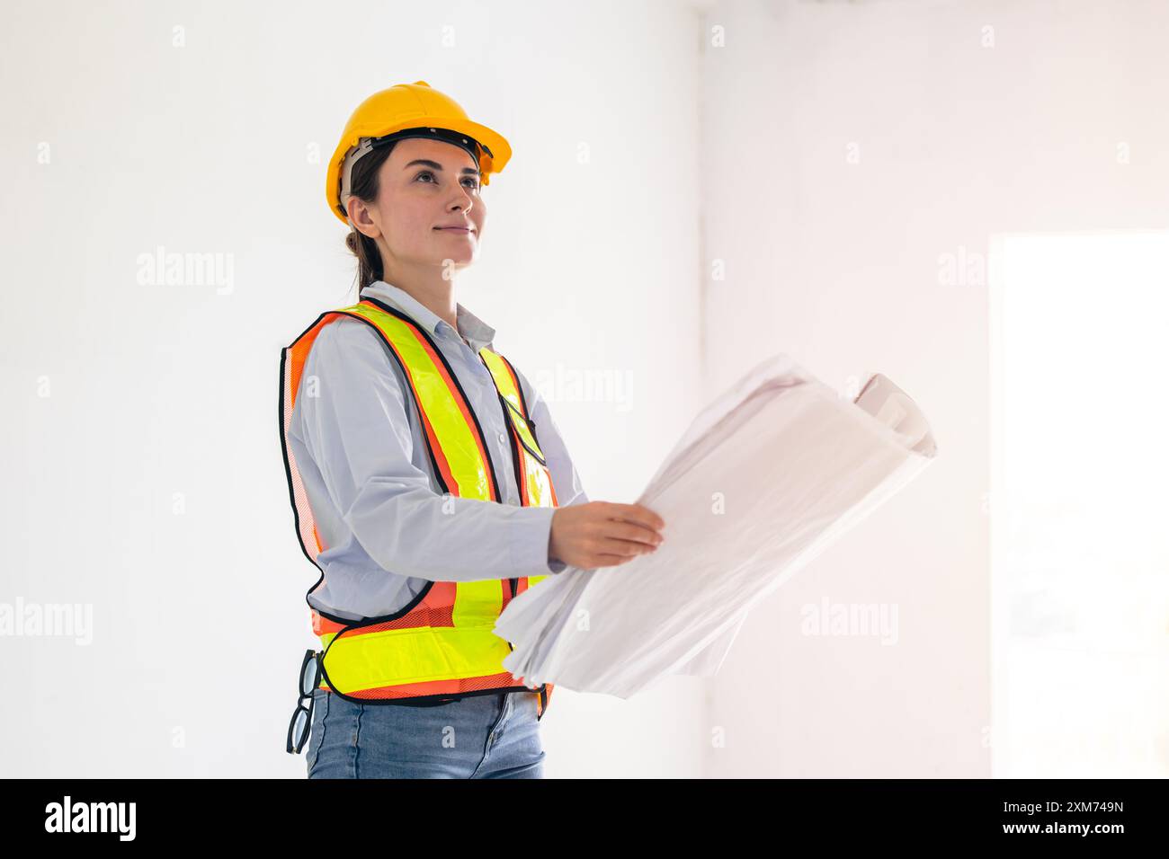 Confident female architect in safety gear holding blueprints and inspecting construction site ...