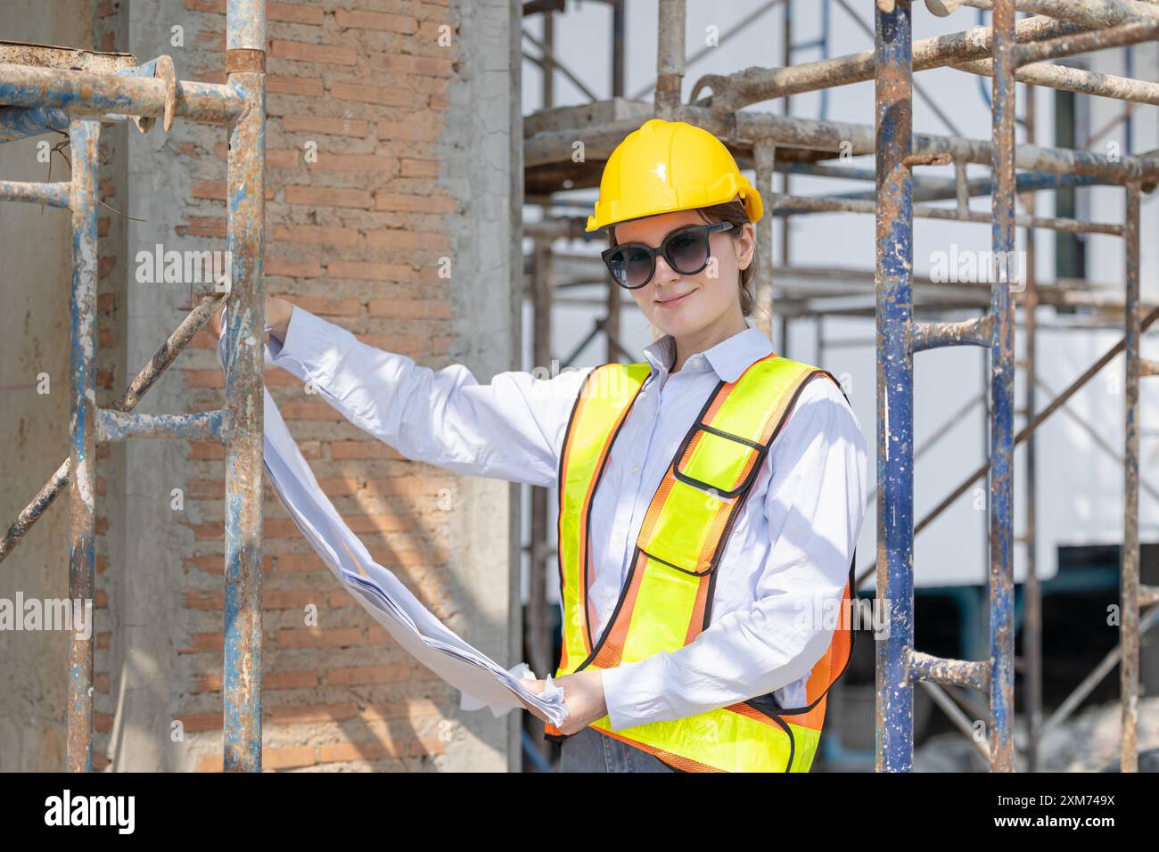 Confident female architect in safety gear holding blueprints and inspecting construction site ...
