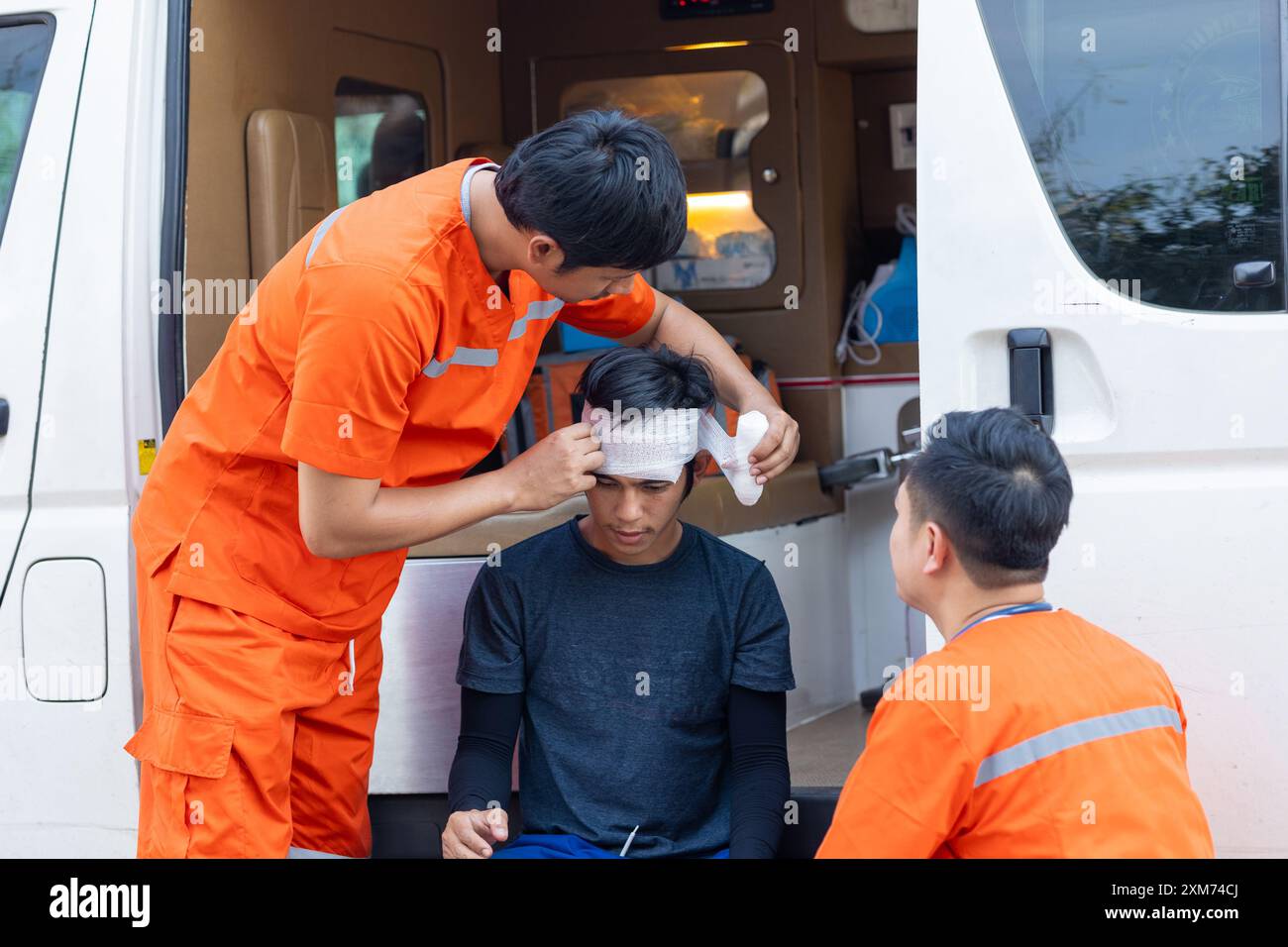 A man with a bandaged head is being helped by two other men in orange ...