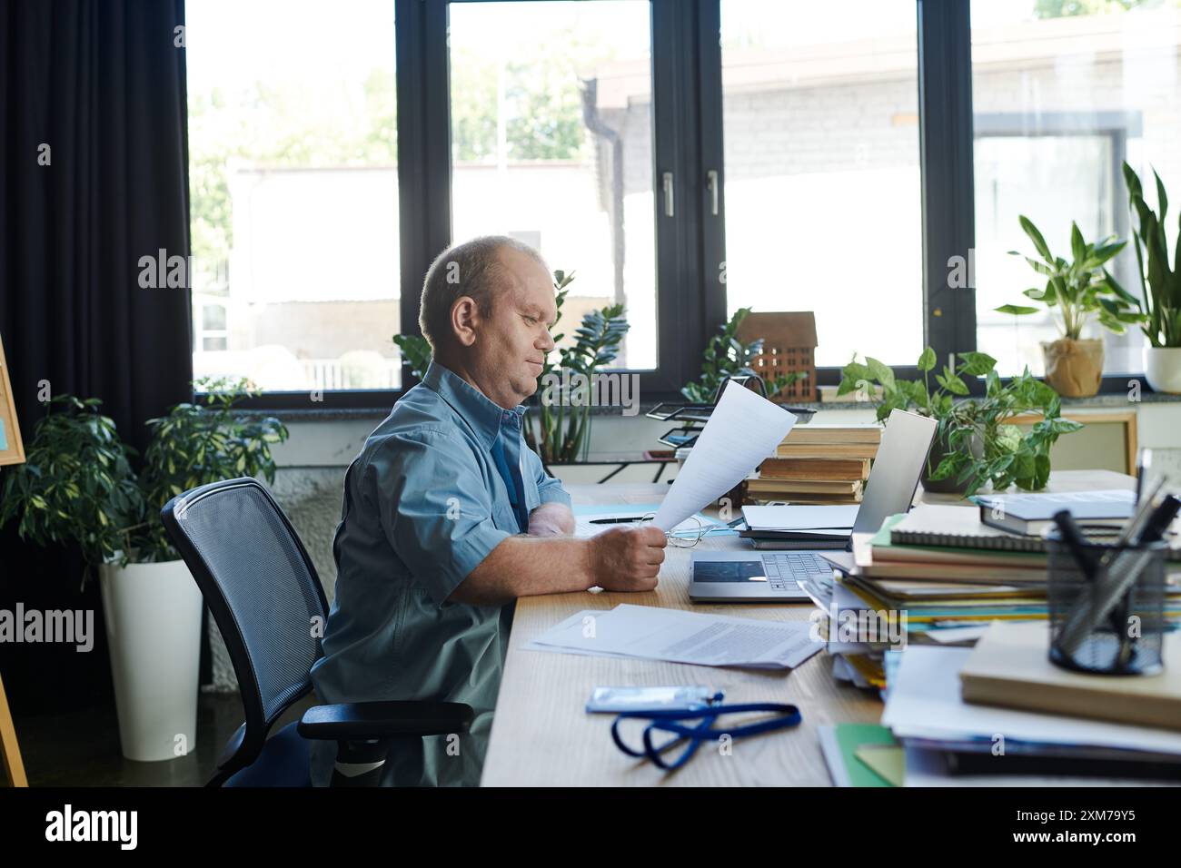 A man with inclusivity sits at a desk reviewing documents while using a ...