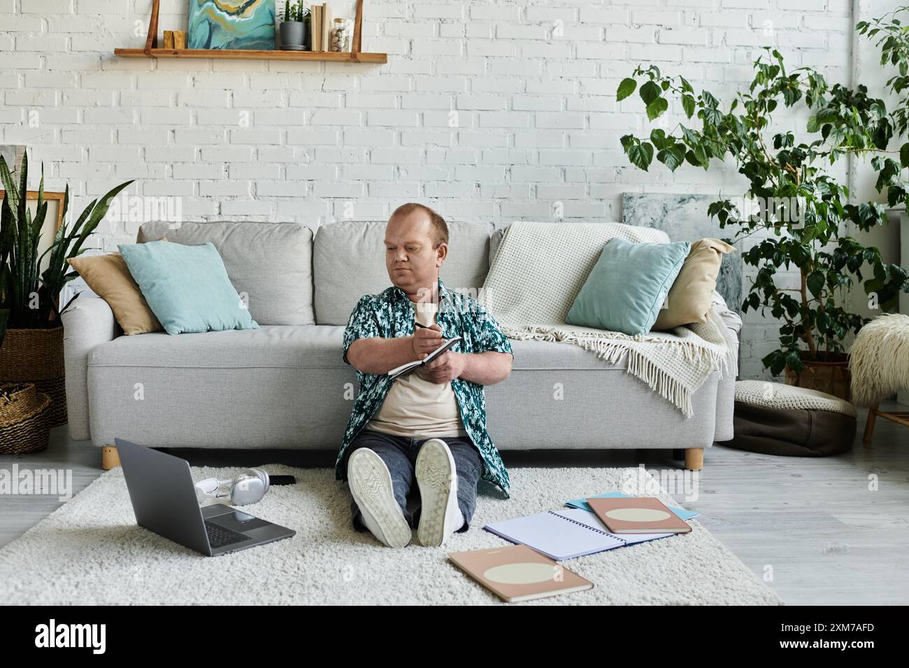 A man with inclusivity sits on the floor of a living room, focused on ...