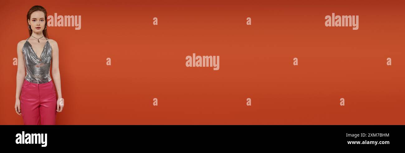 A young woman poses against a bright orange background, wearing a ...