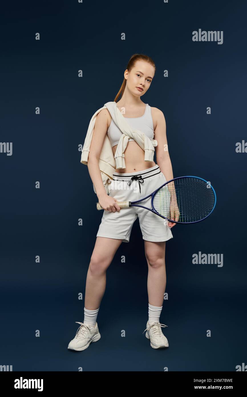 A young woman in tennis attire holds a racket and poses against a ...