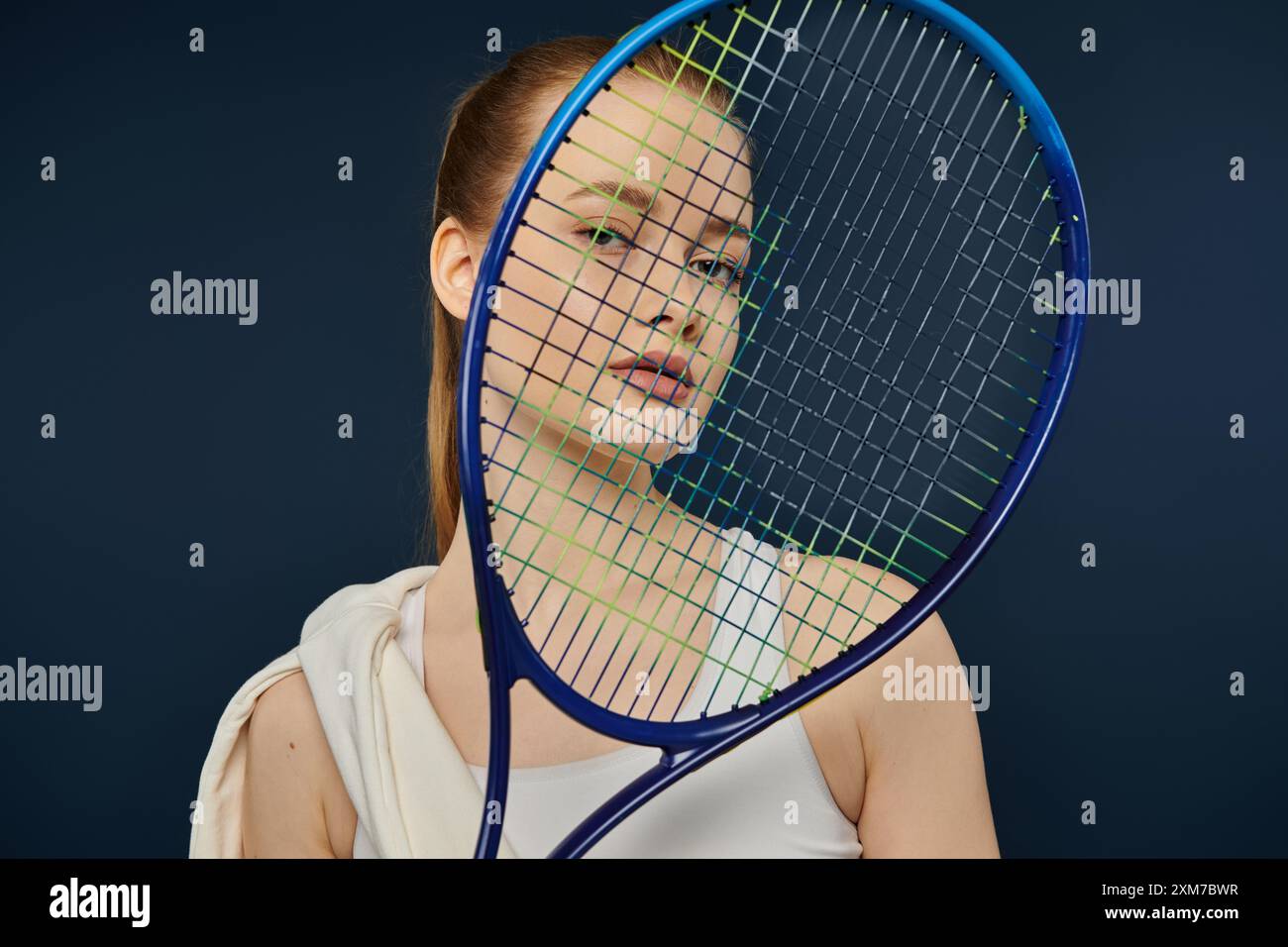 Young woman gracefully poses with tennis racket against bold backdrop ...