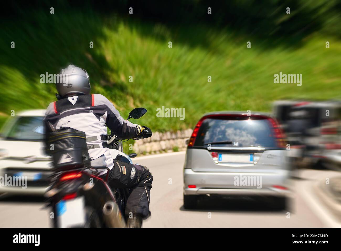 Italy - July 21, 2024: A motorcyclist rides dangerously close to a car ...