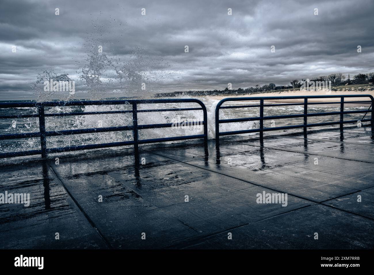 A powerful ocean wave crashes against a sturdy railing positioned along ...