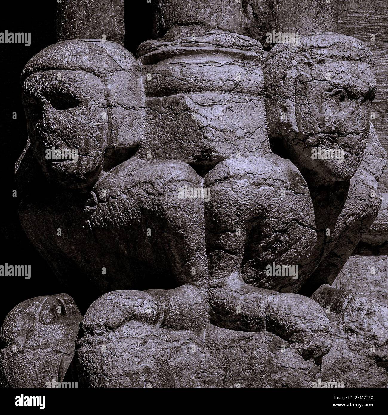 Two of three seated figures huddled at base of column at cathedral in ...