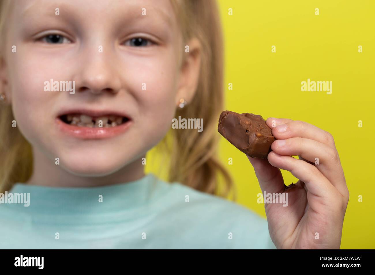 Beautiful little girl eating a chocolate bar on a yellow background ...