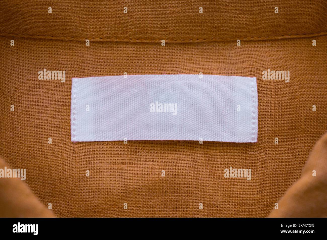 White blank clothing tag label on brown linen shirt fabric texture ...