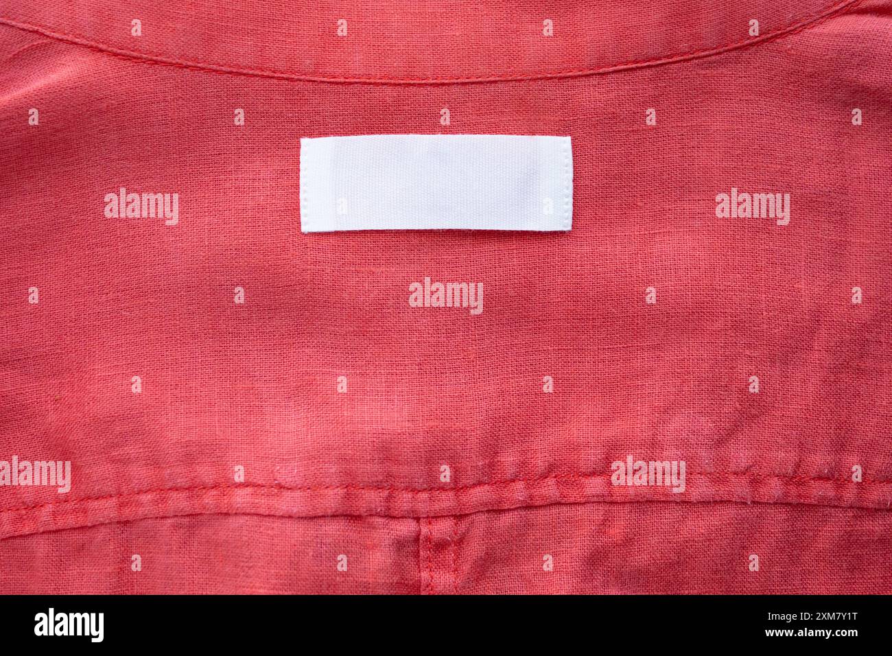 White blank clothing tag label on red linen shirt fabric texture ...