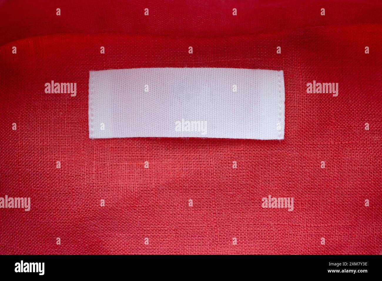 White blank clothing tag label on red linen shirt fabric texture ...