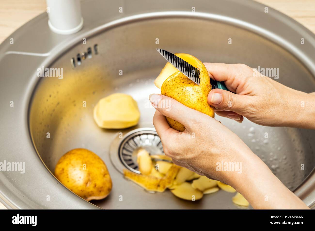 housewife peels fresh potatoes with a knife in the kitchen. peel the ...
