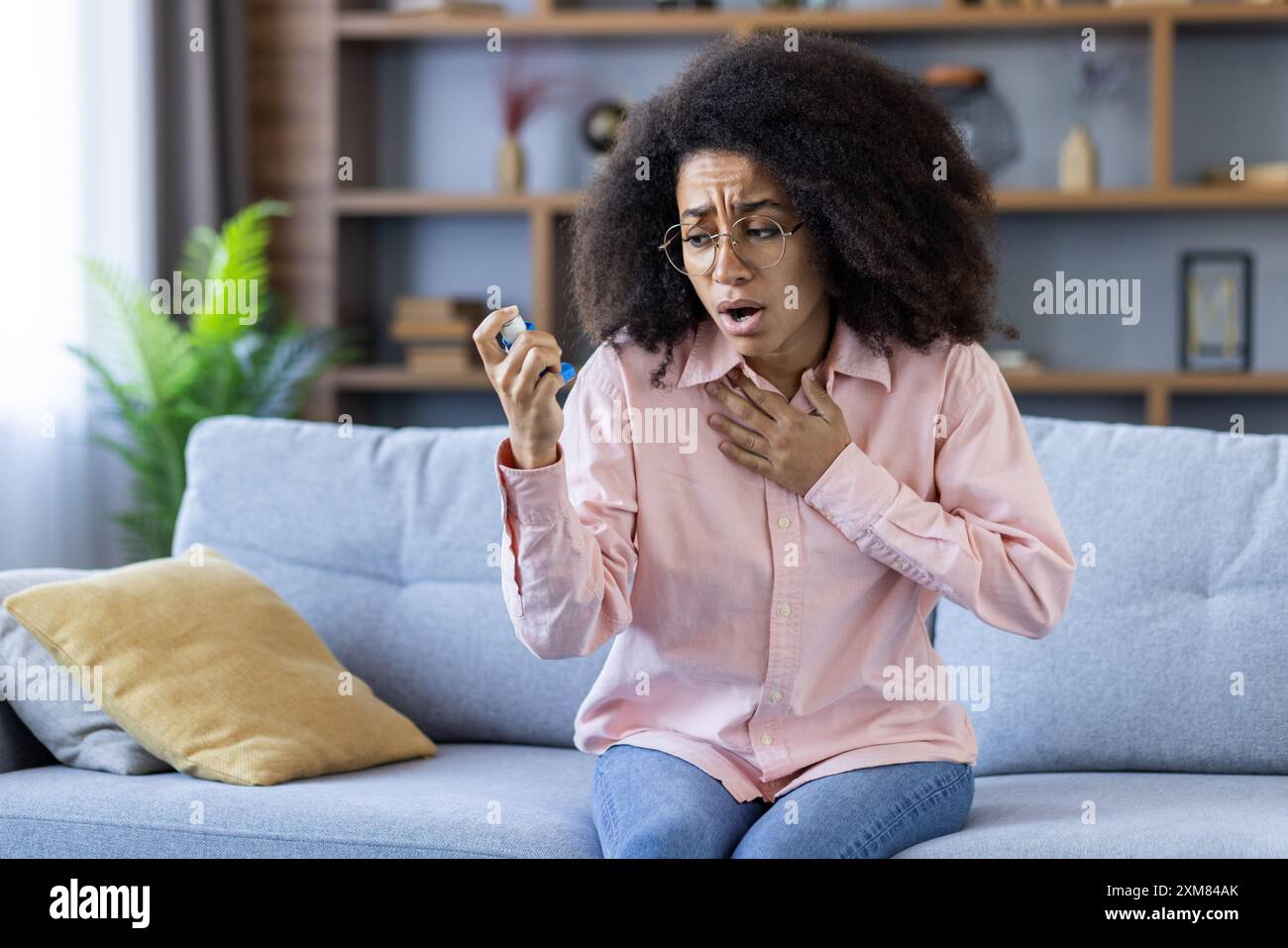 Young woman suffering from asthma attack using inhaler while sitting on ...