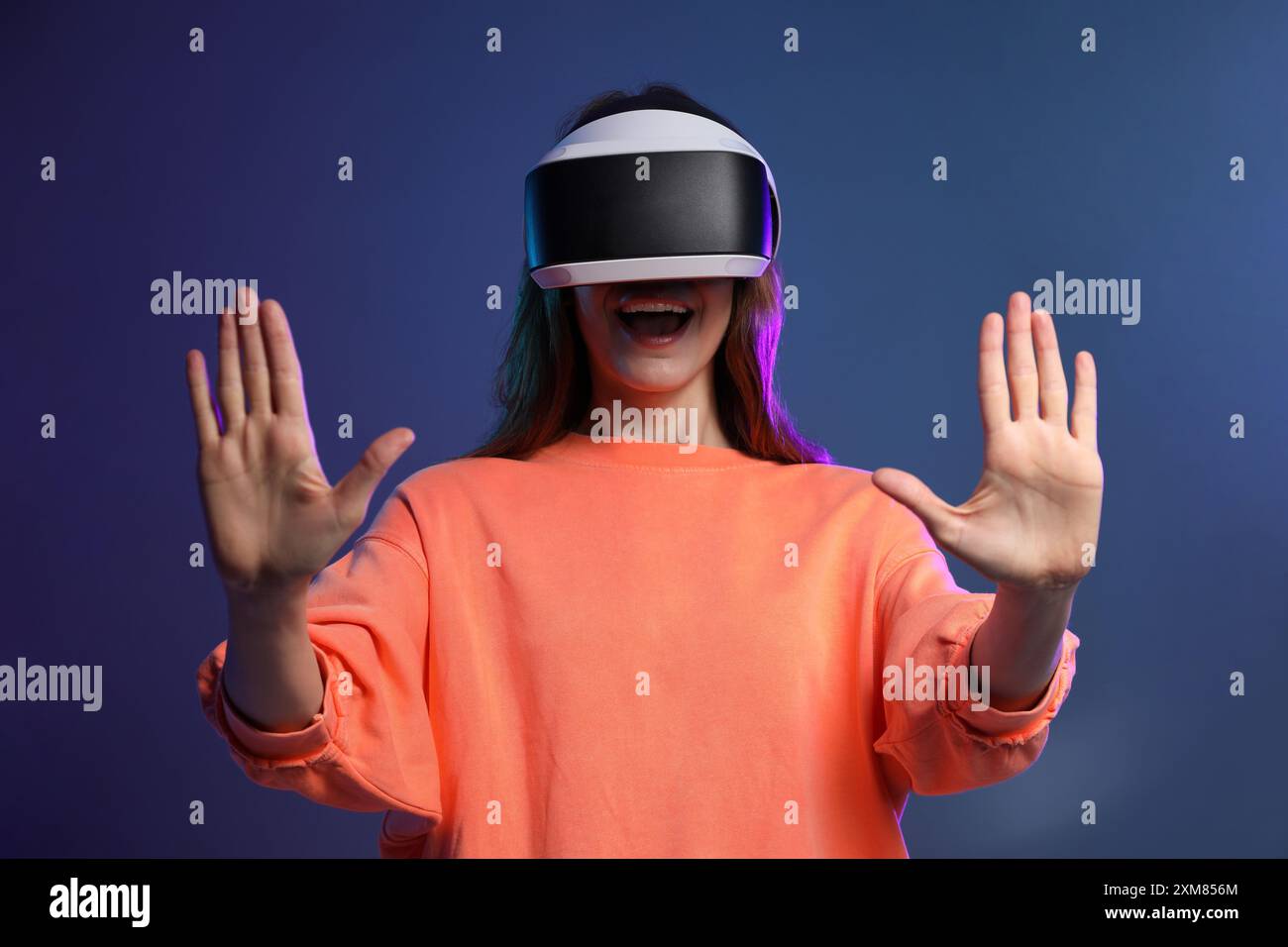 Emotional woman using virtual reality headset on dark blue background ...