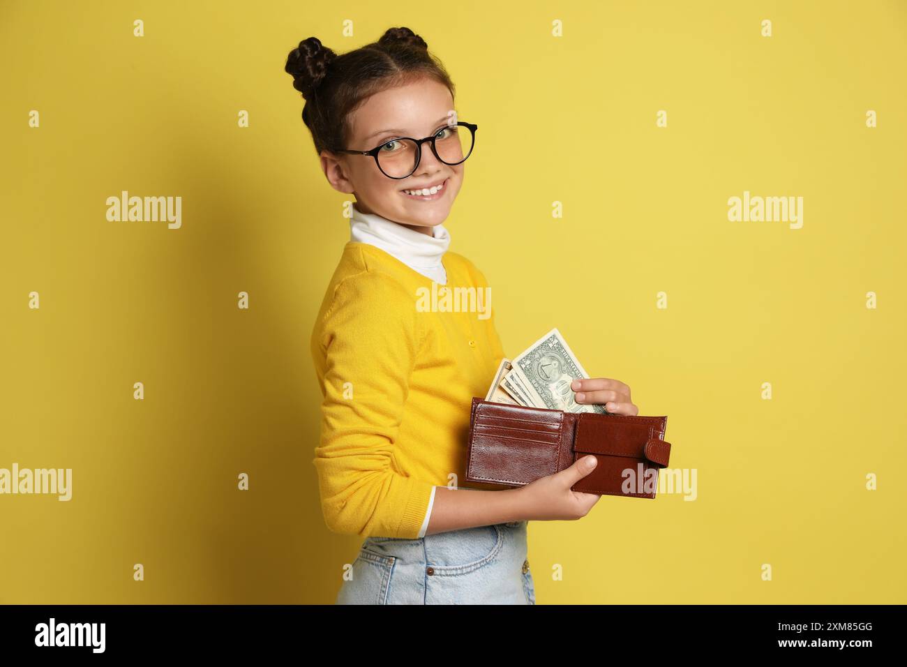 Pocket money. Cute girl with wallet and dollar banknotes on yellow ...