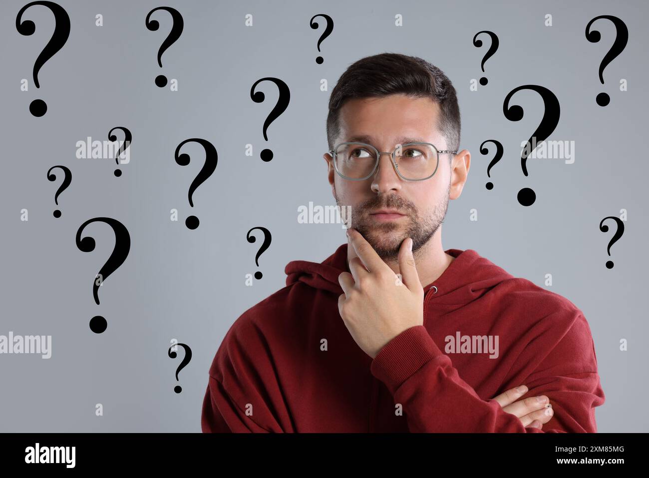 Thoughtful man and question marks on grey background Stock Photo - Alamy