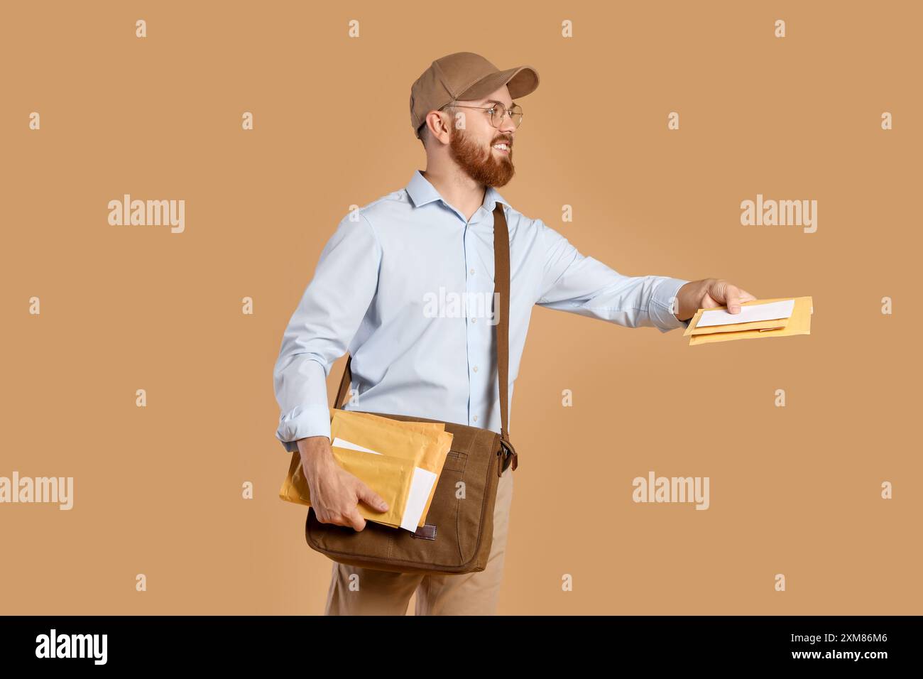 Happy young postman with leather bag delivering letters on brown ...