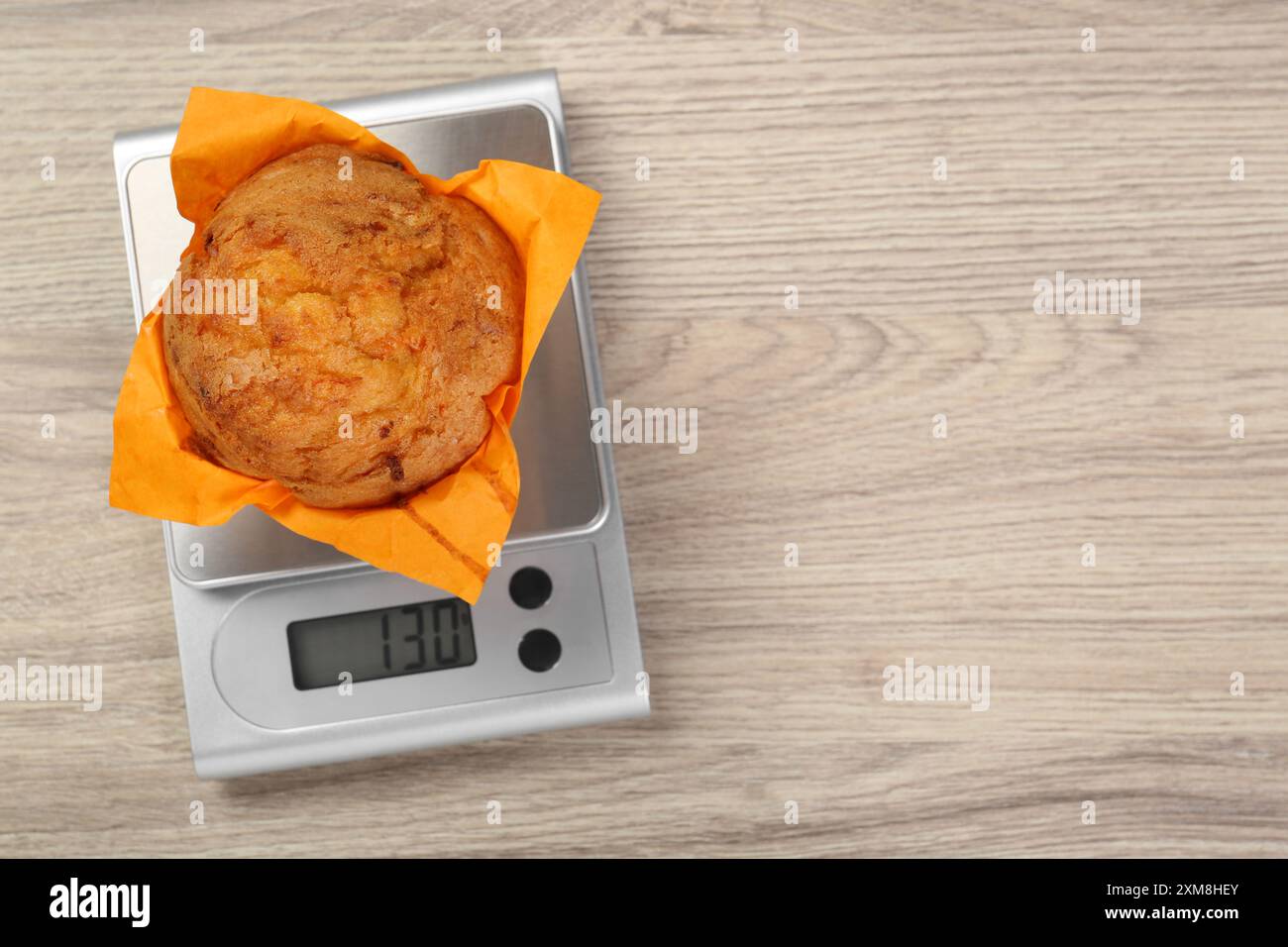 Kitchen scale with muffin on light wooden table, top view. Space for ...