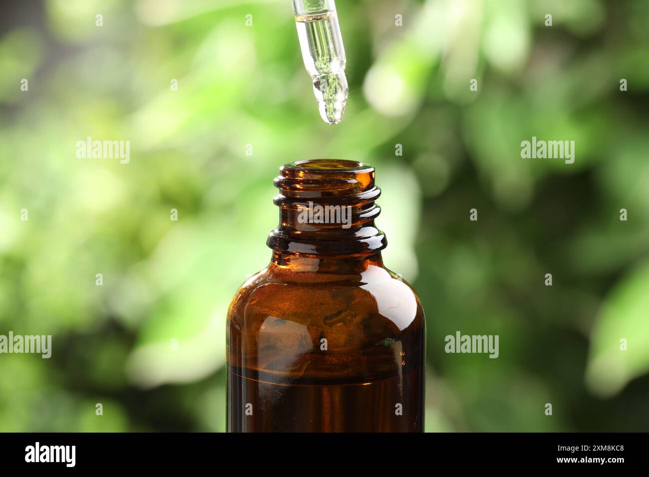 Essential oil dripping from pipette into bottle against blurred green ...