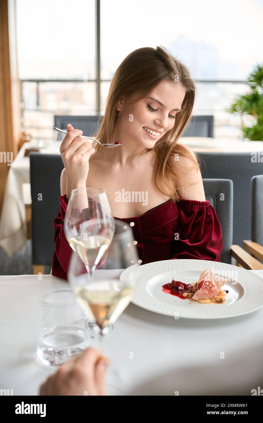 Smiling young woman looking down shyly while eating dessert on dating ...