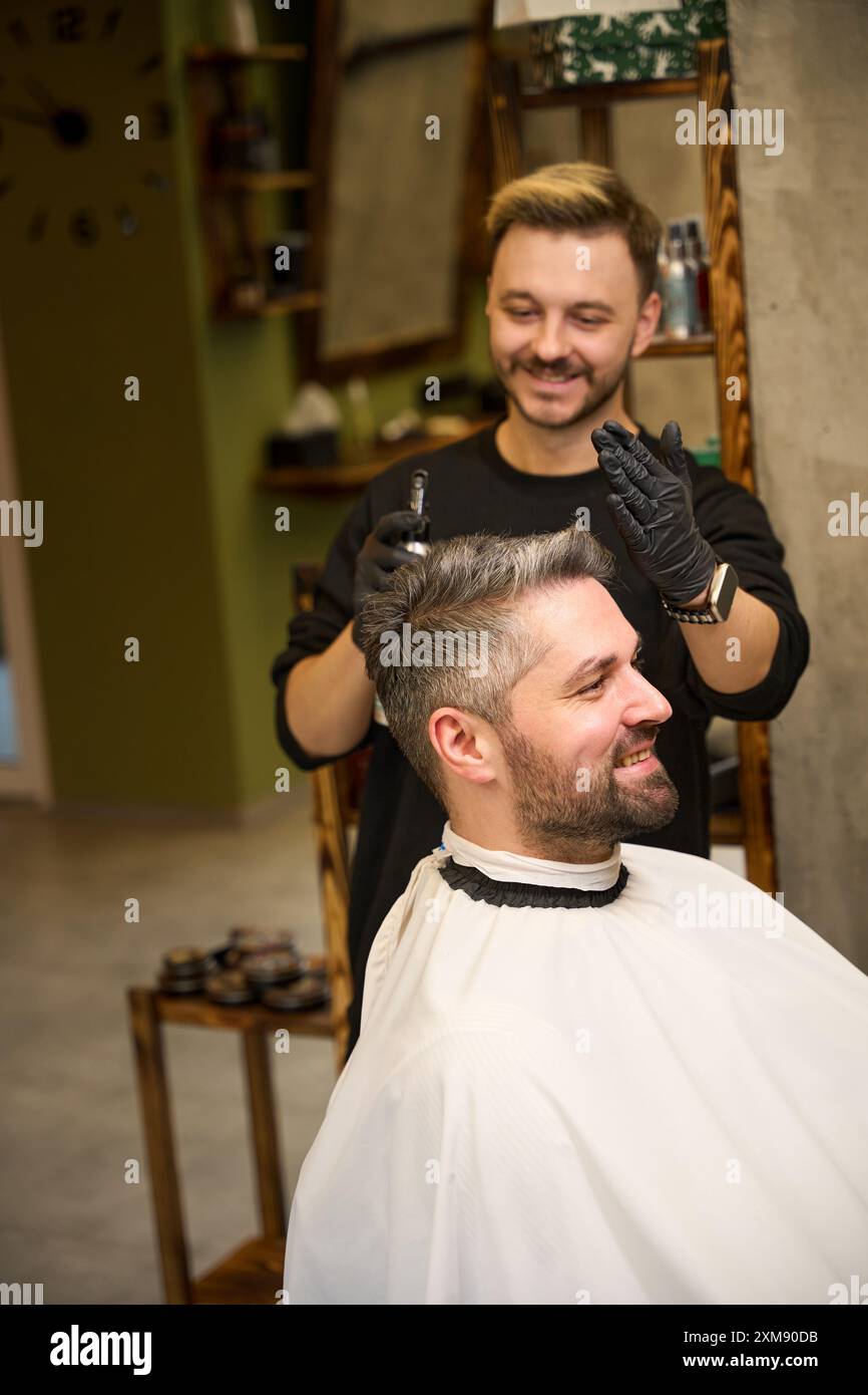 Positive bearded barber spraying fixing liquid into the man haircut ...