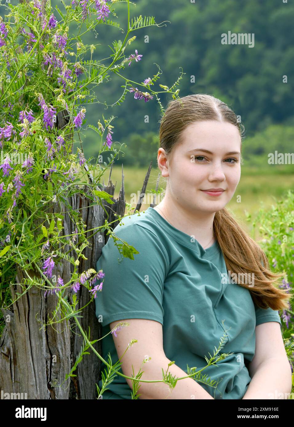 Sitting on rustic, log seat, female teen looks calmly towards camera ...