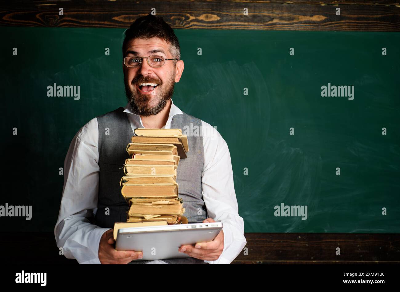 Male university teacher with laptop and textbook in front of blackboard ...