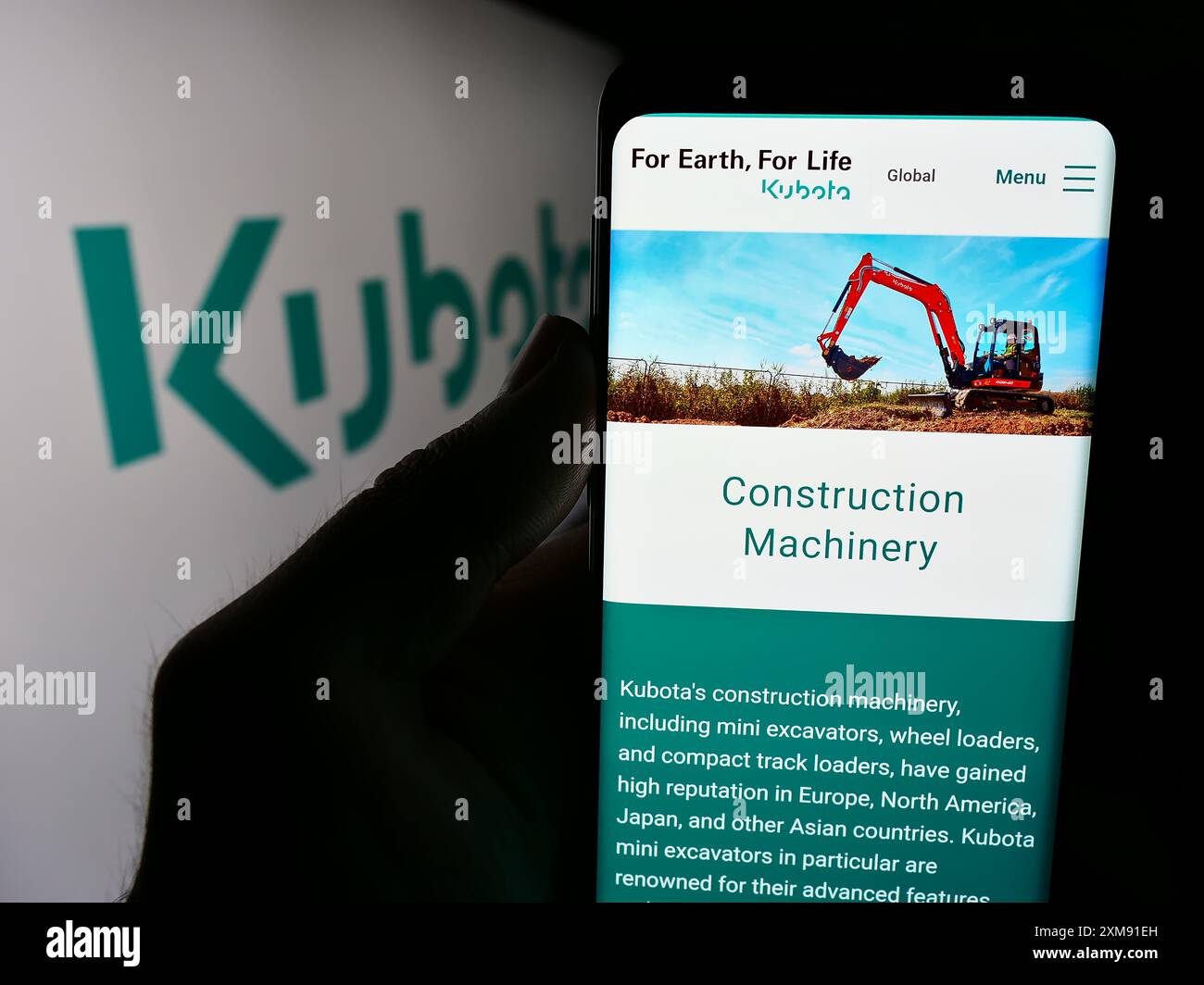 Person holding mobile phone with website of Japanese heavy equipment ...