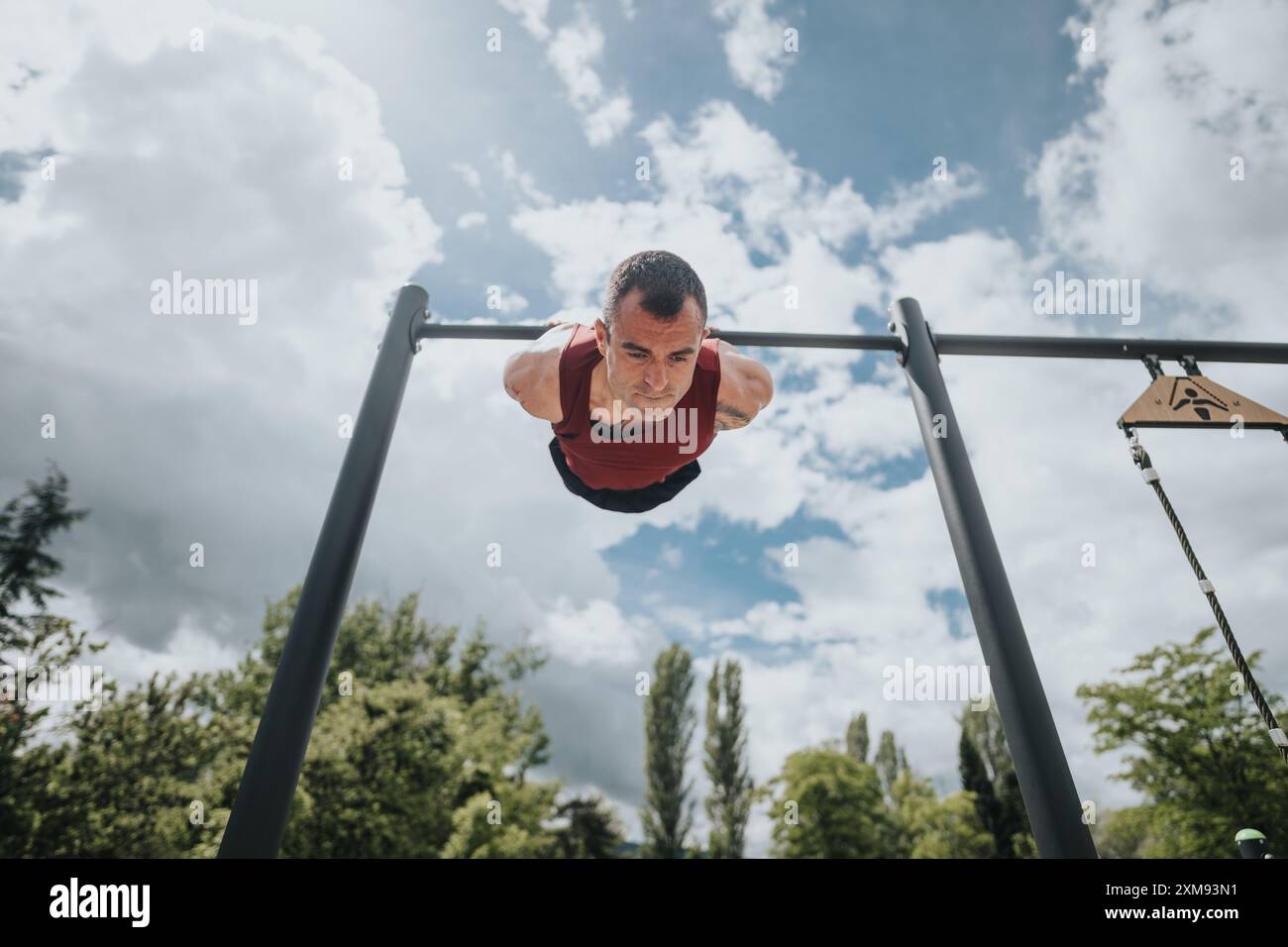 Focused athlete performing pull-ups in an urban park under a sunny sky ...