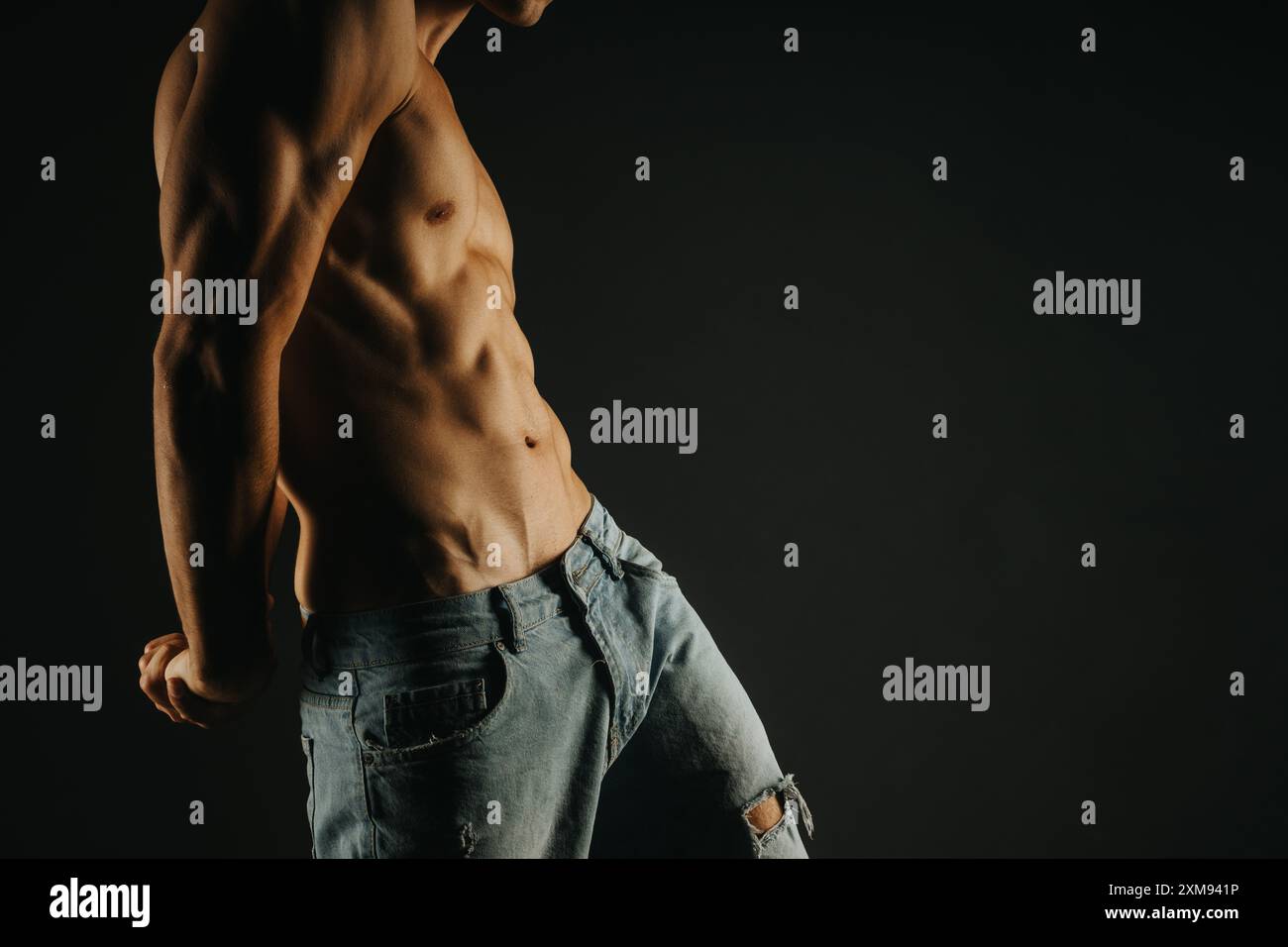 Fit man showing toned abs and muscles in moody lighting wearing ...