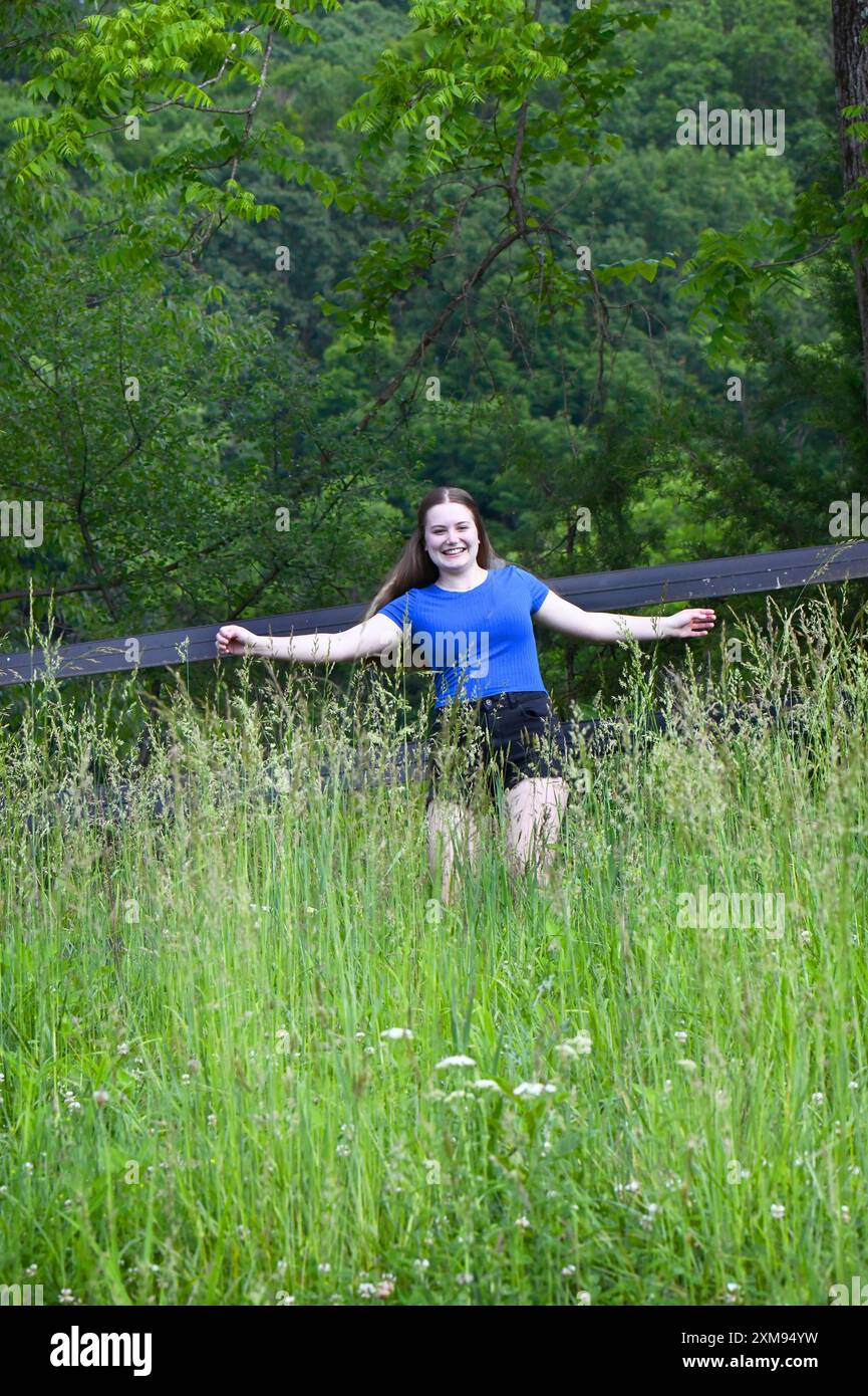 Teenager playful swirls in field of tall grass. Fence is behind her ...