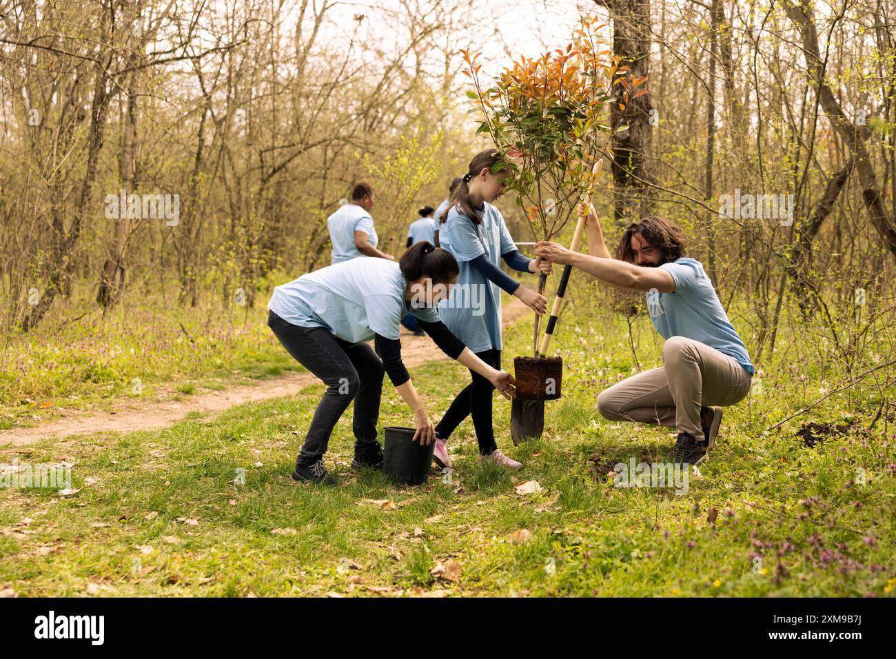Volunteers and a child planting a tree and covering hole in the ground ...
