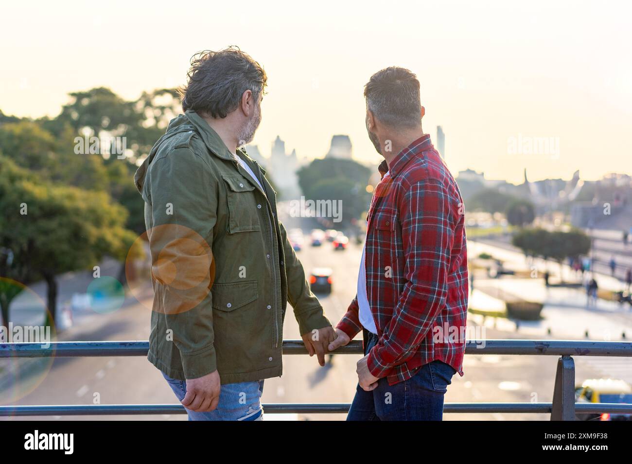 Two men, a gay couple, are holding hands while looking out at the ...