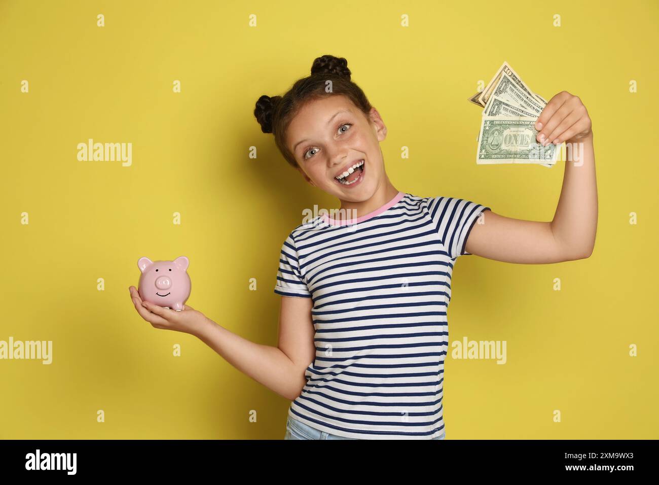 Pocket money. Cute girl with piggy bank and dollar banknotes on yellow ...