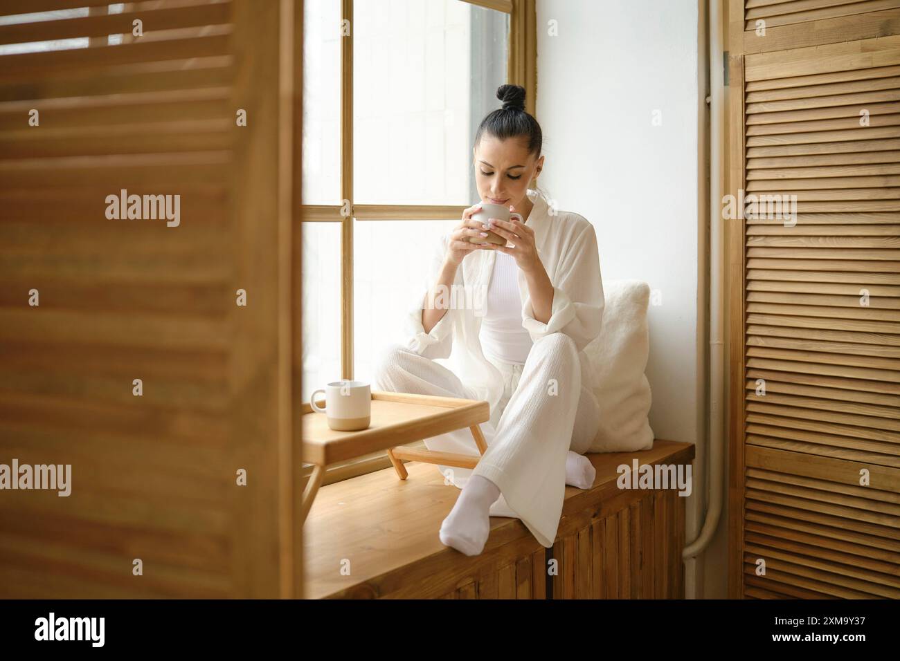 Pretty woman enjoys a peaceful morning, sipping coffee while sitting on ...
